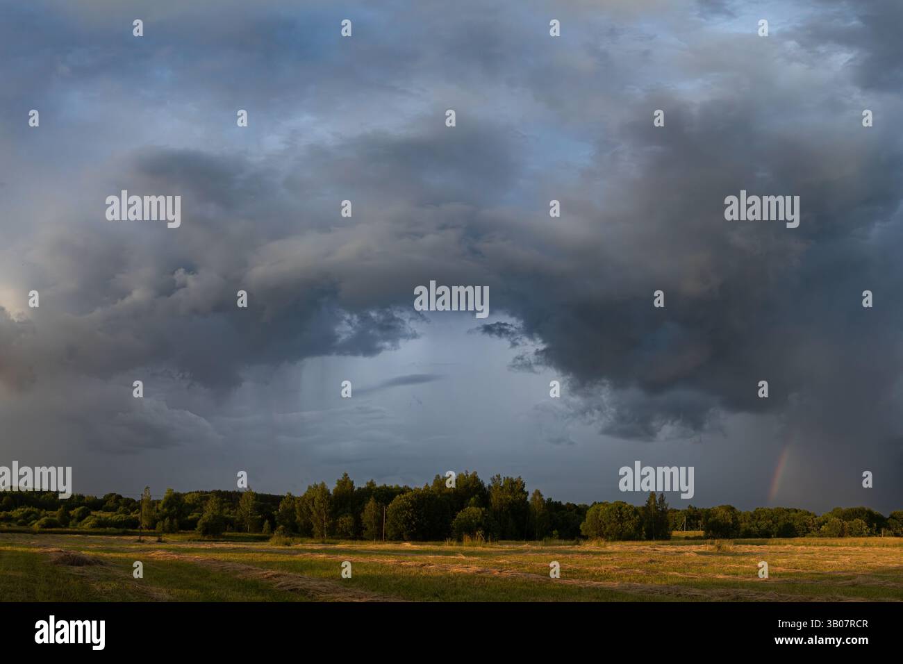 Dark, turbulent storm clouds sweep across the sky while a faint rainbow ...