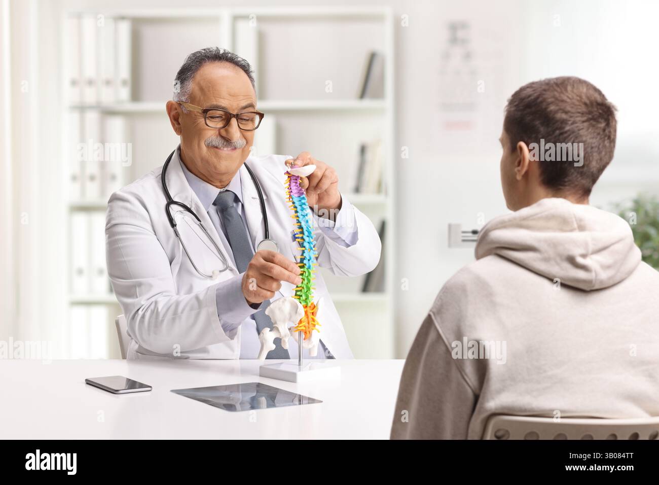 Mature male doctor explaining a cervical spine model to a young male ...