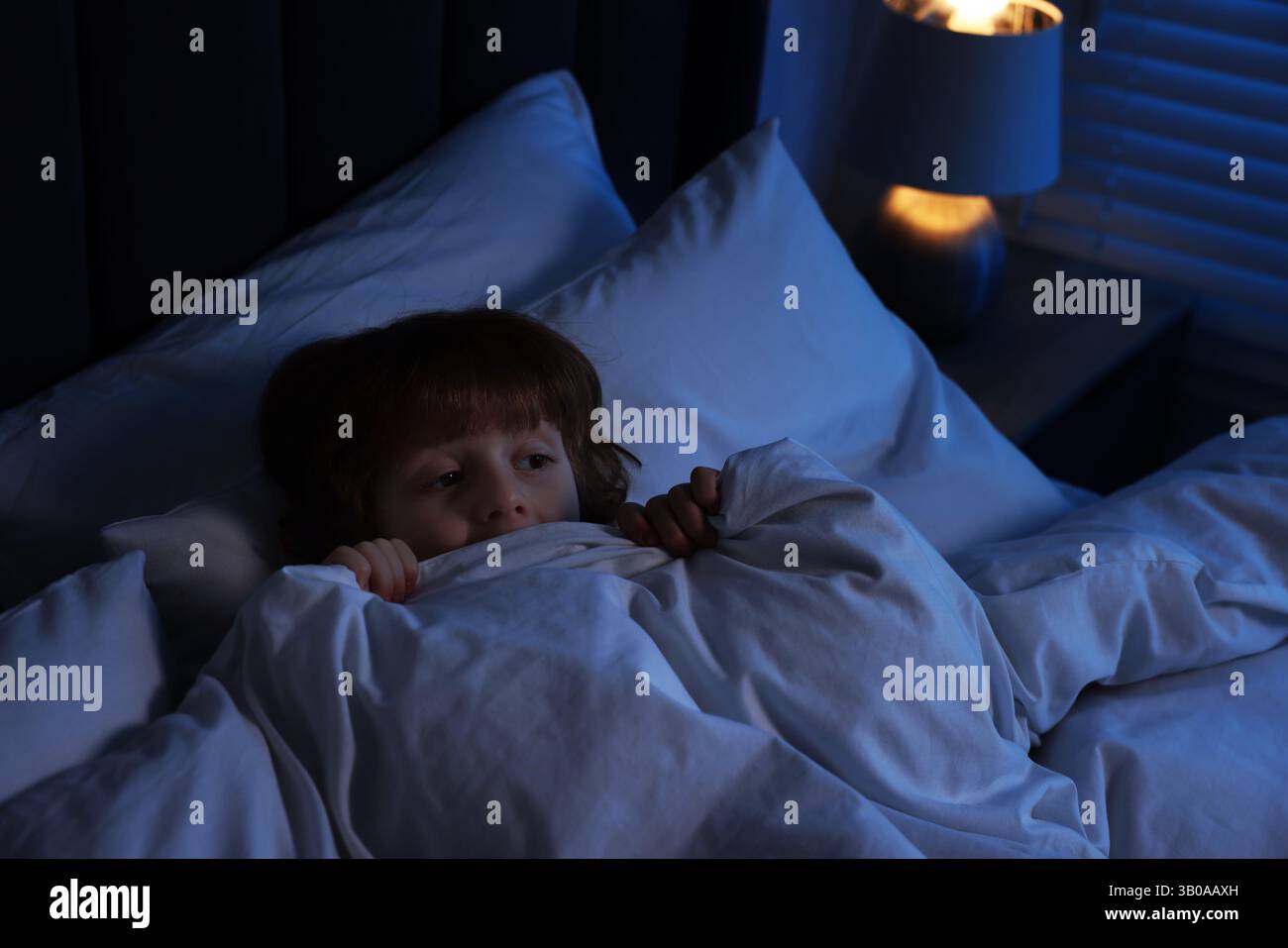 Scared boy hiding under duvet in bed at night Stock Photo - Alamy