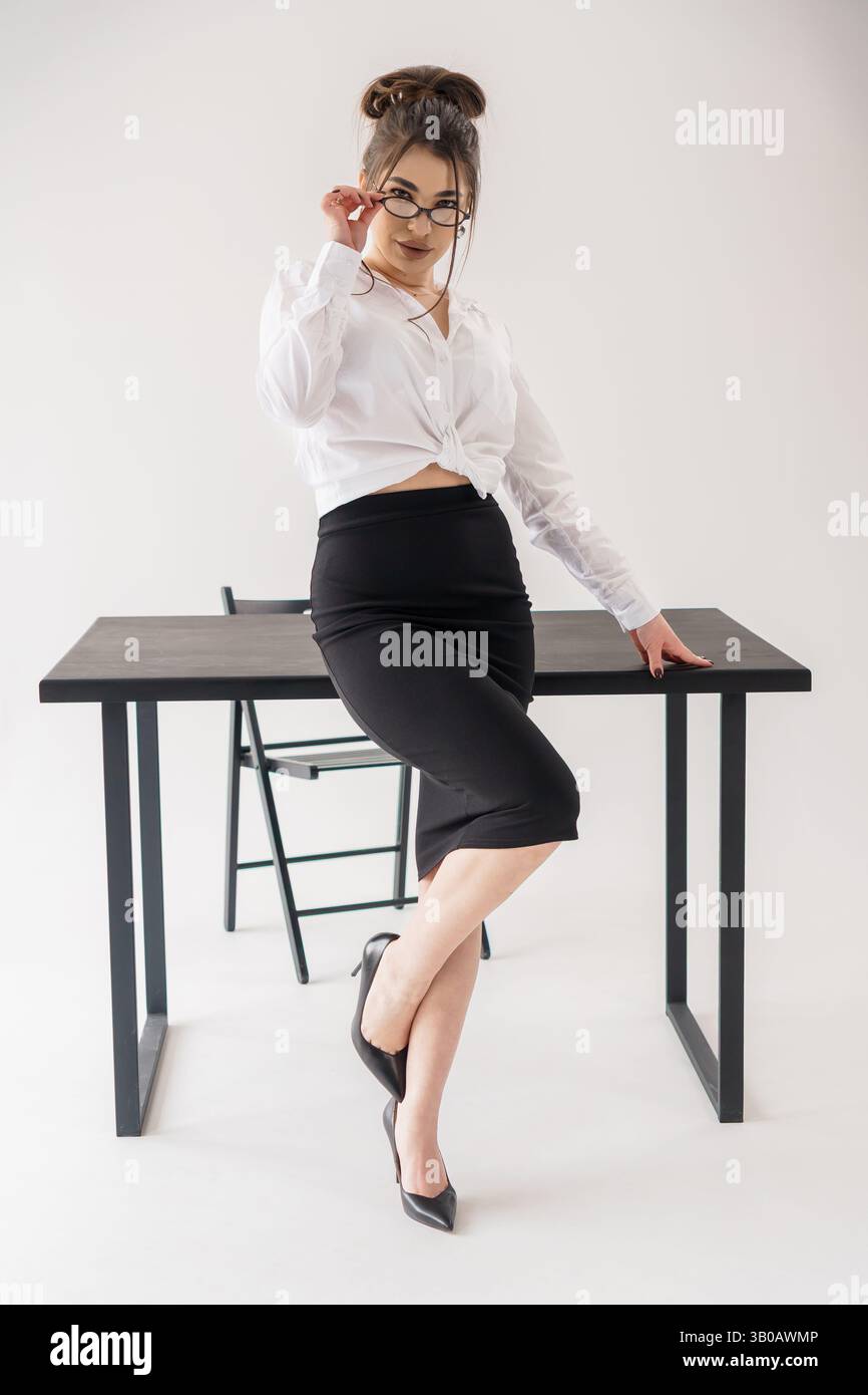 Confident young woman in business attire leaning on table with playful ...