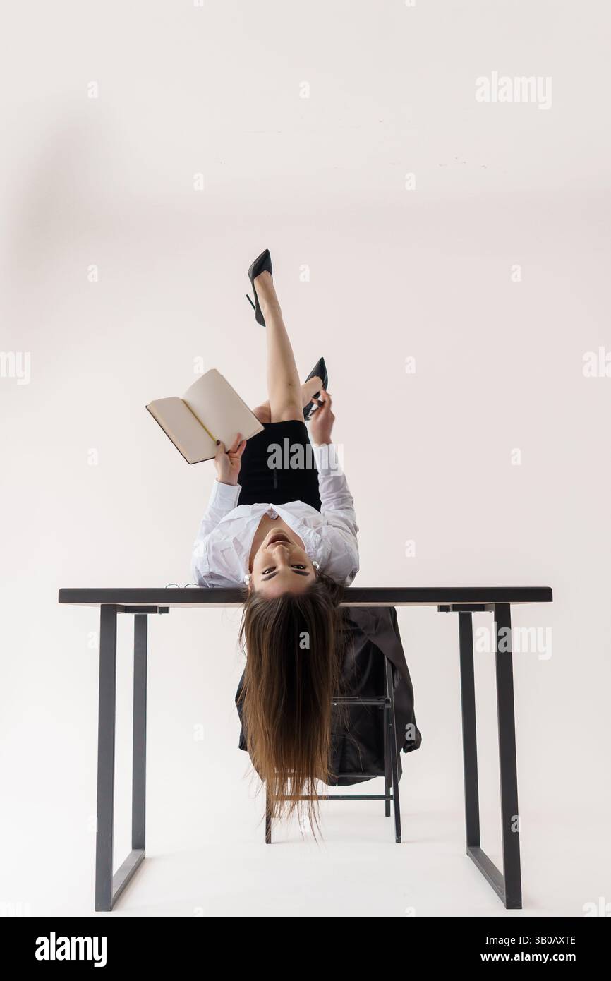 Upside-down businesswoman reading a book with legs on the table in a ...