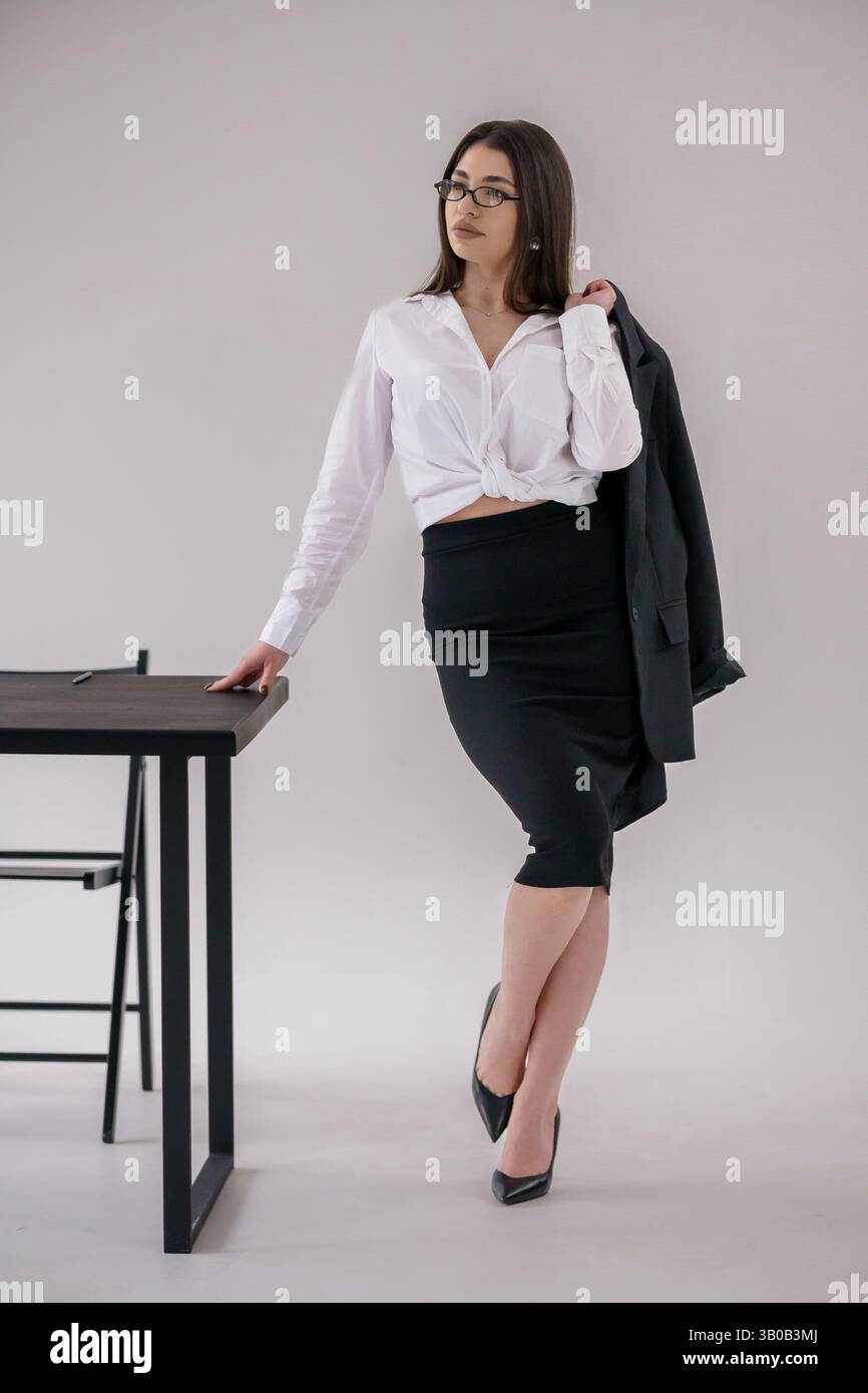 Confident businesswoman leaning on desk with a black skirt and white ...