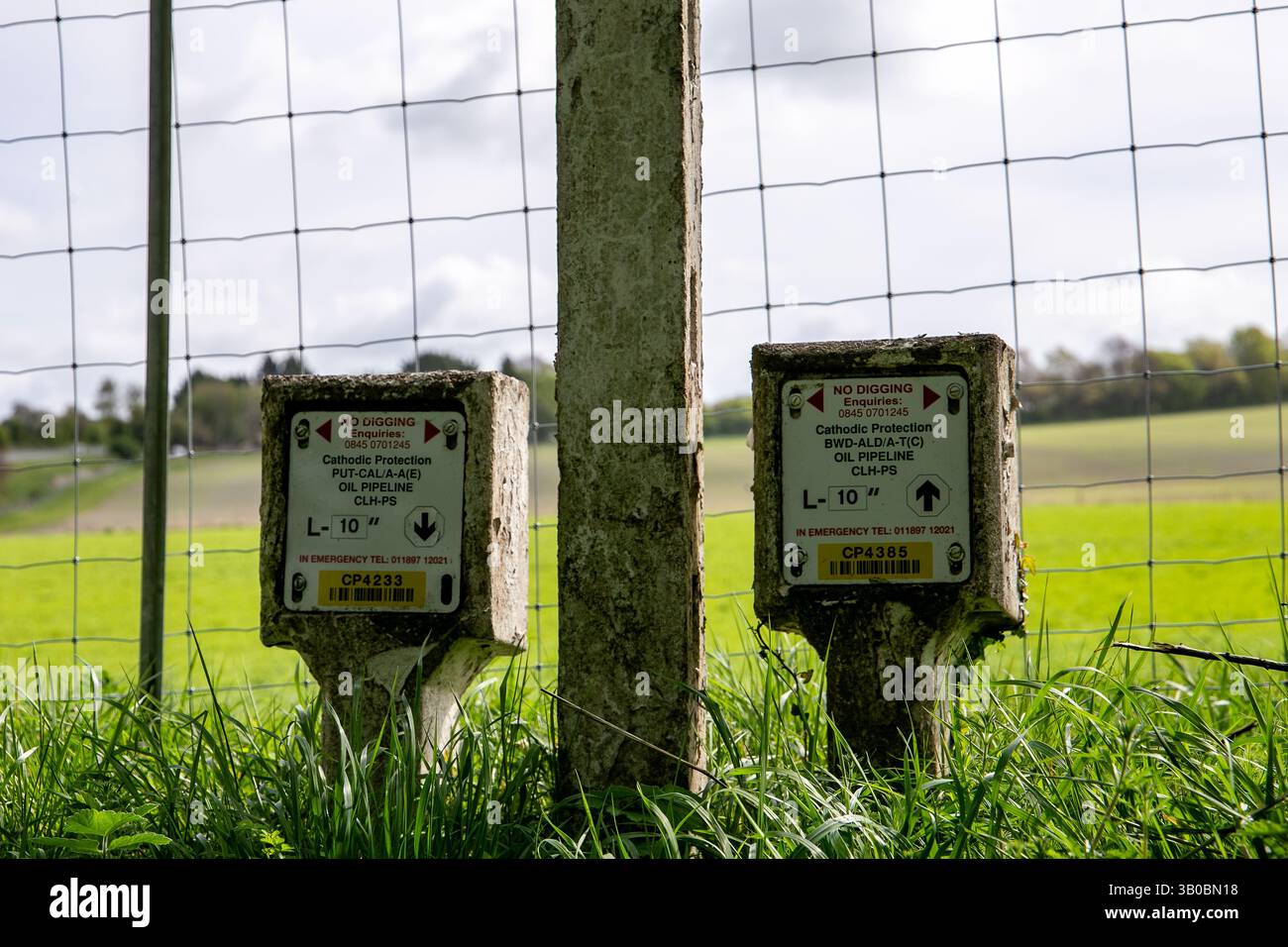 Two cathodic protection markers in a grassy field by a wire fence ...