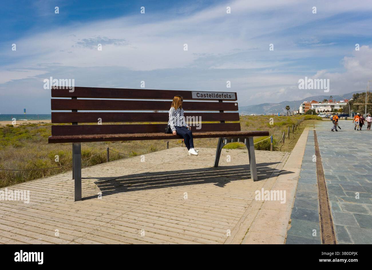 A woman in her 40's sits on an oversized bench on Castelldefels beach ...