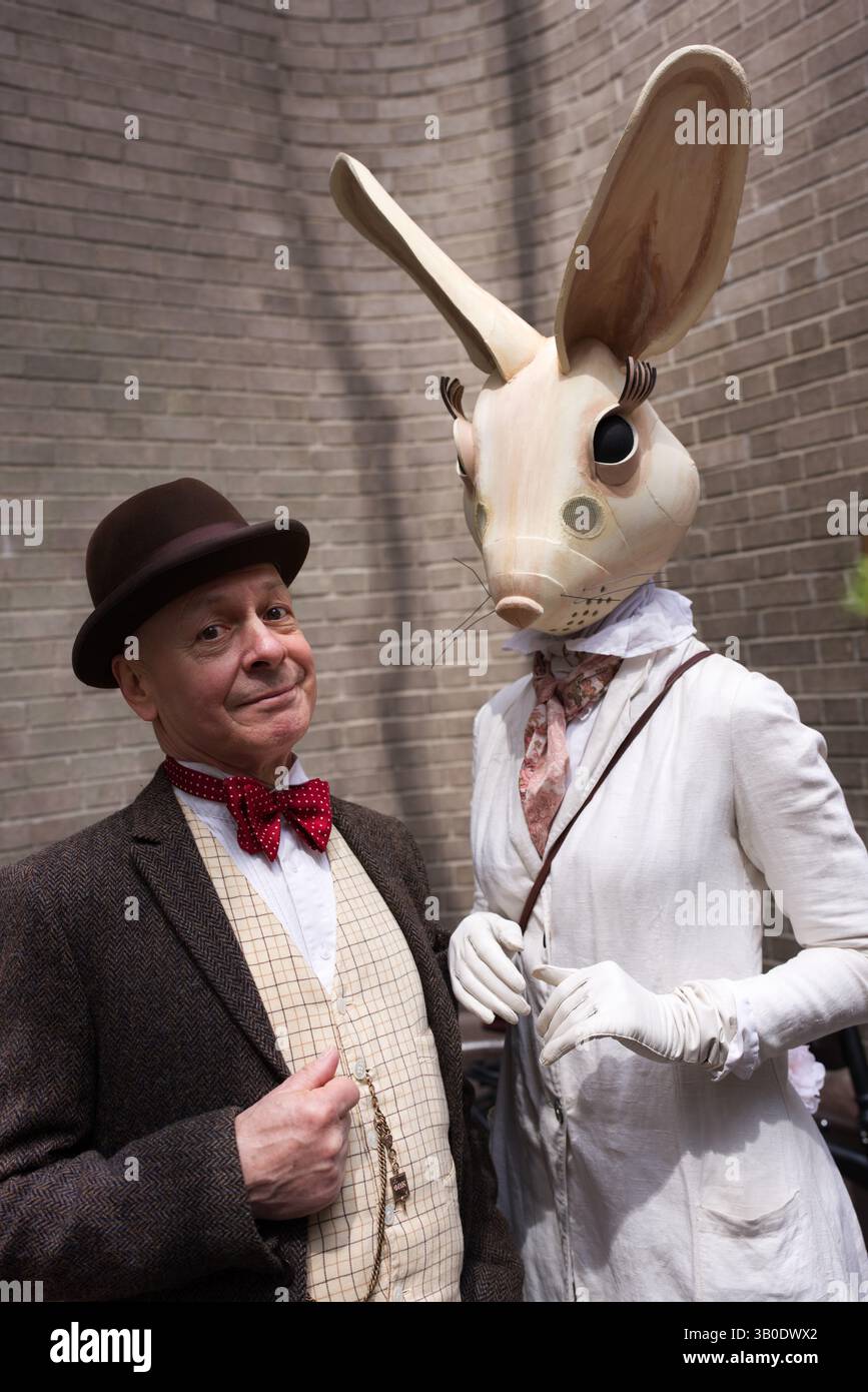 A man in a tweed suit and bowler hat stands beside a person wearing a ...