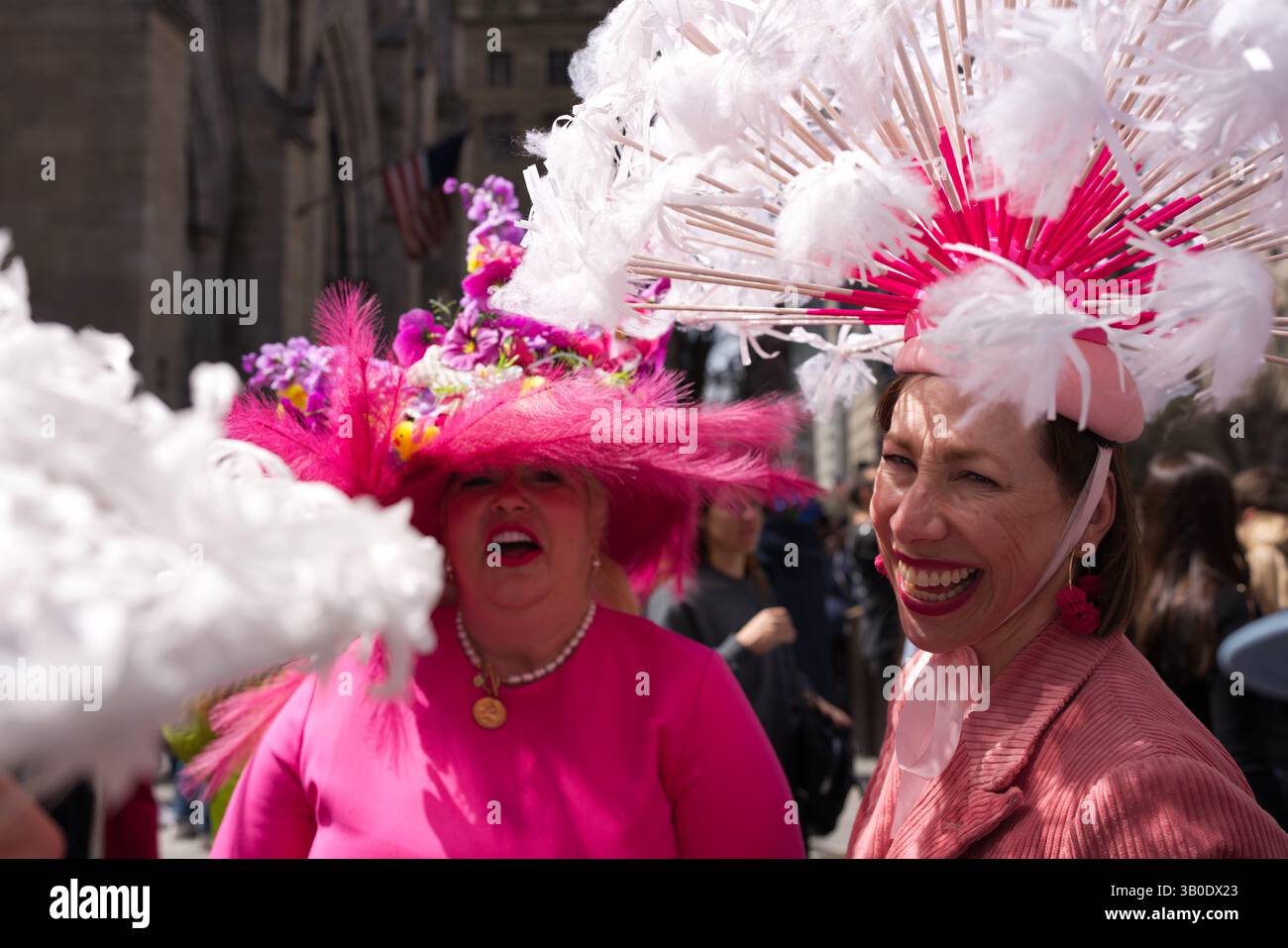 Two women in vibrant pink outfits wear elaborate, oversized hats ...