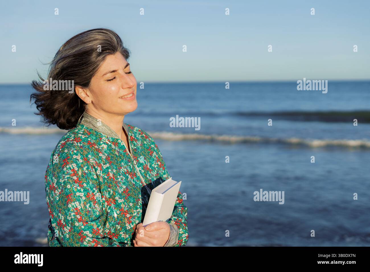 Mature female writer with closed eyes enjoying a sea breeze while ...