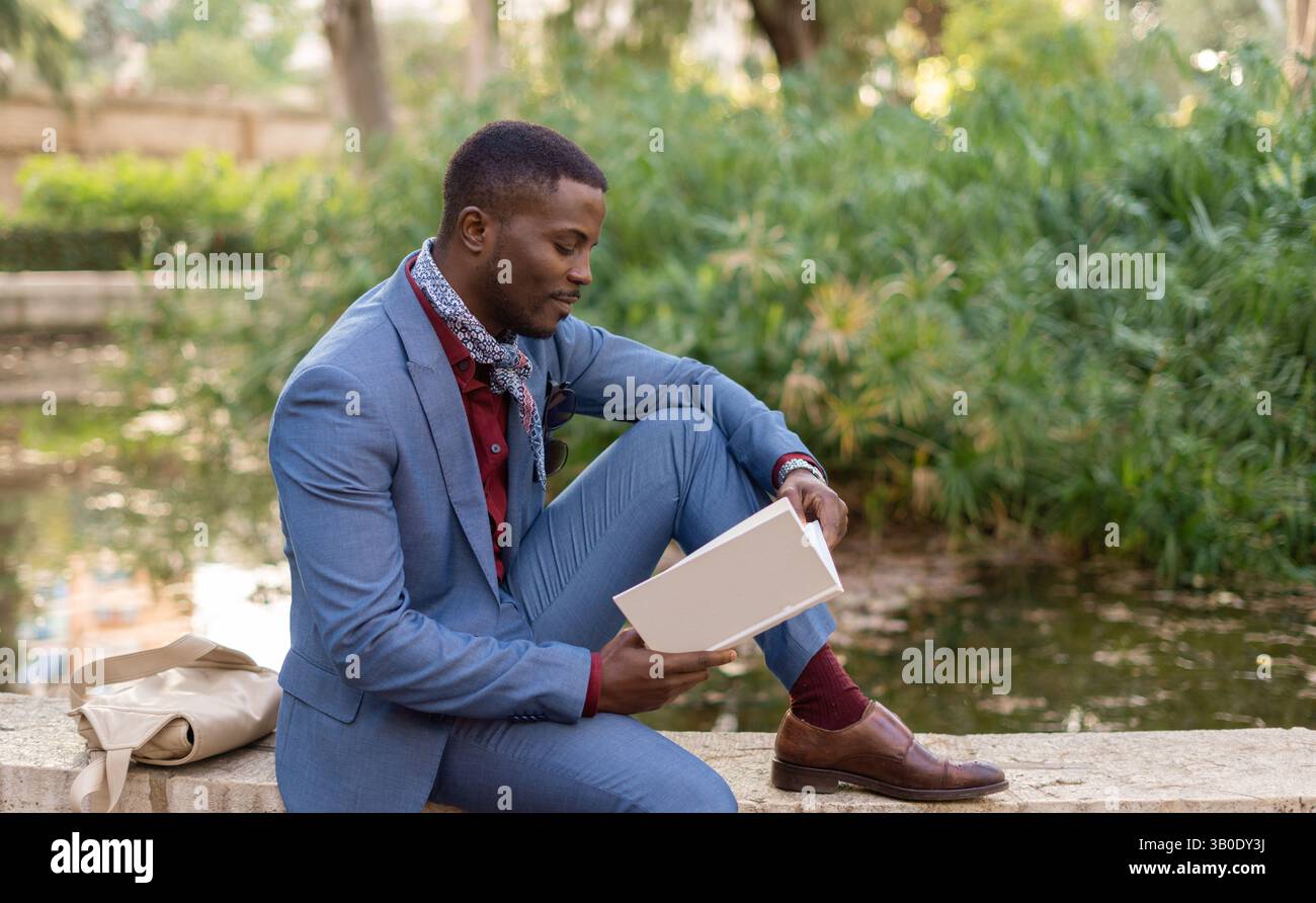 An Elegant Man Reading a Book by the Water While Dressed in a Stylish ...