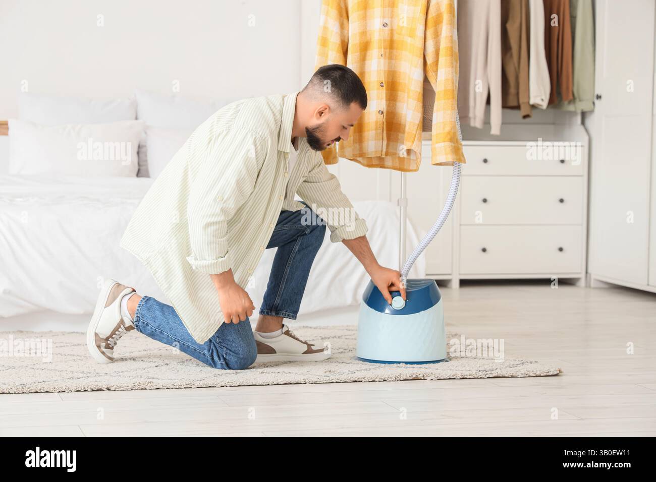 Young man turning on steamer in bedroom Stock Photo - Alamy