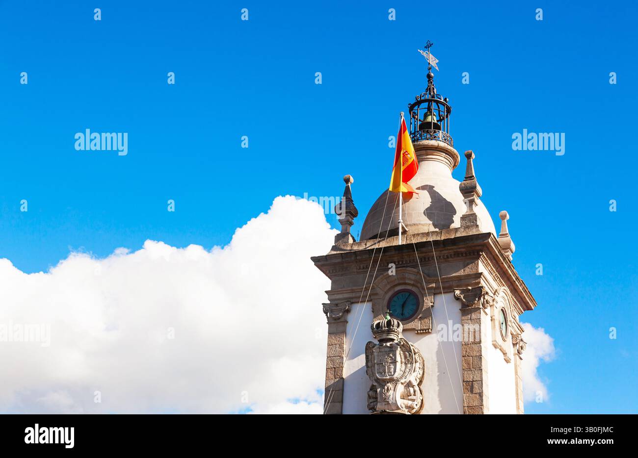 An ancient clock tower with a Spanish flag against a blue sky with ...
