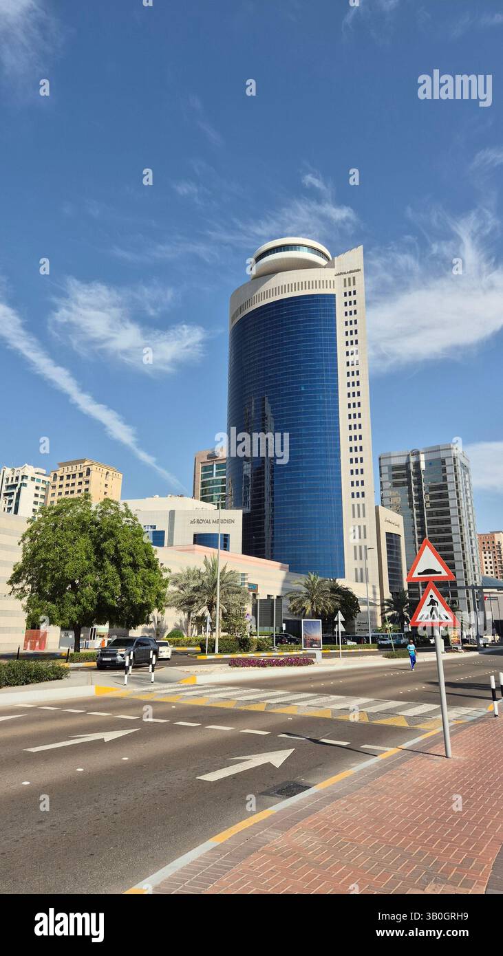 A busy street in Abu Dhabi features a striking blue skyscraper among ...