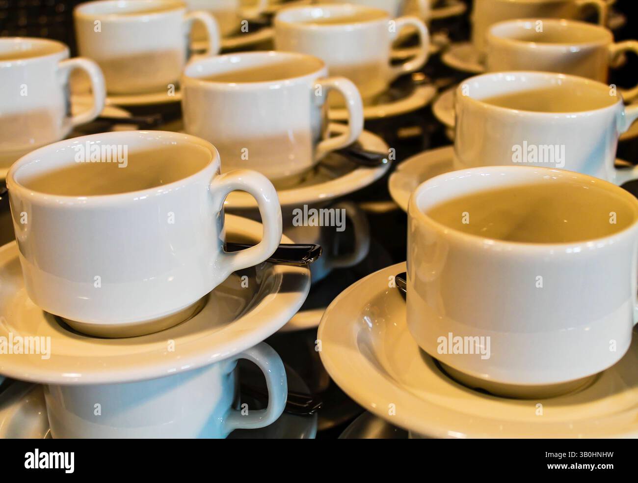 A close-up view of multiple white coffee cups arranged on saucers ...