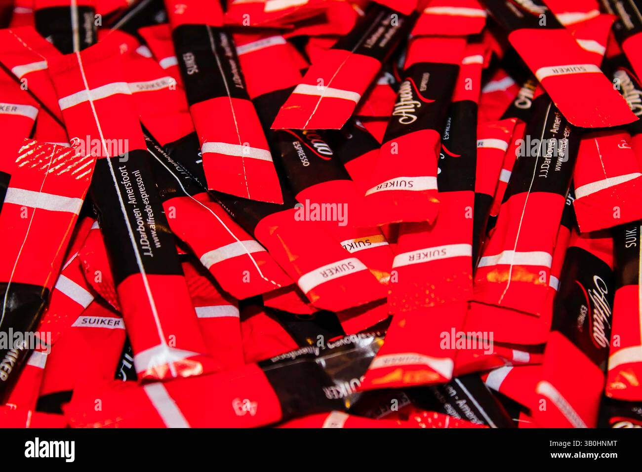 A close-up view of numerous red and black sugar packets piled together ...