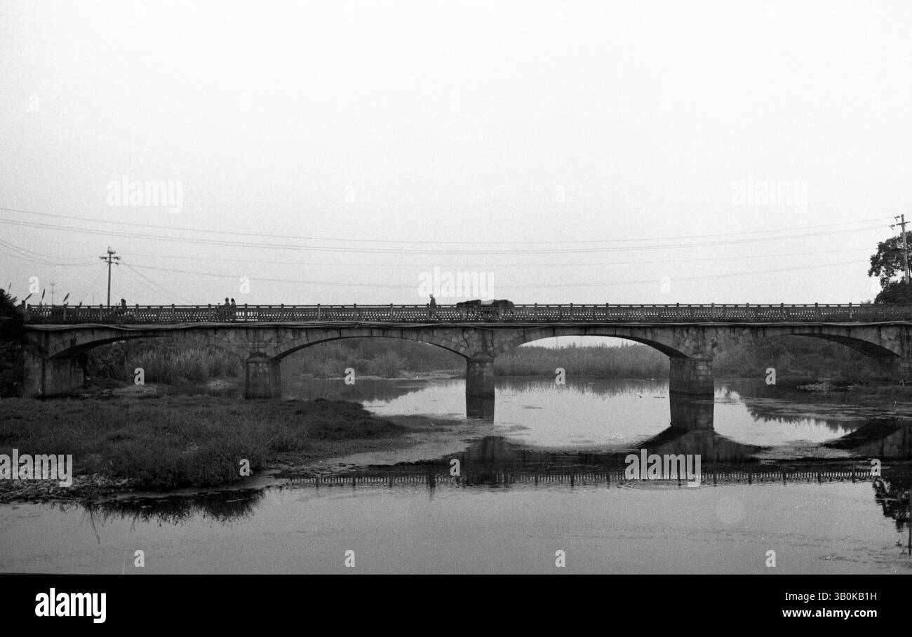 Farmer Leading Ox across Stone Arch Bridge over Reflective River in ...