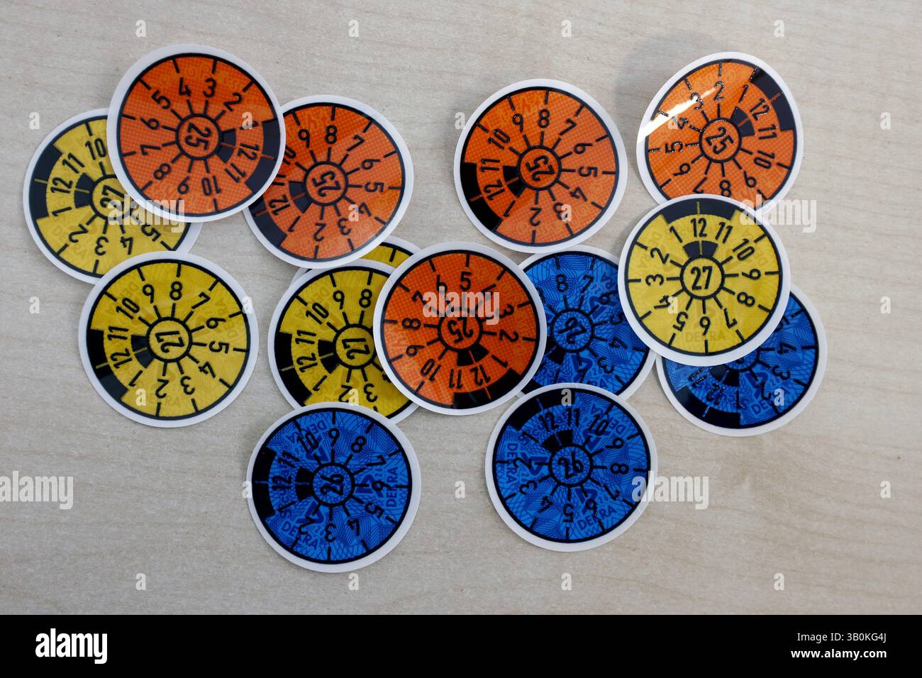 Tuev Tüv Plaketten in den Farben gelb, blau und orange liegen auf einem ...