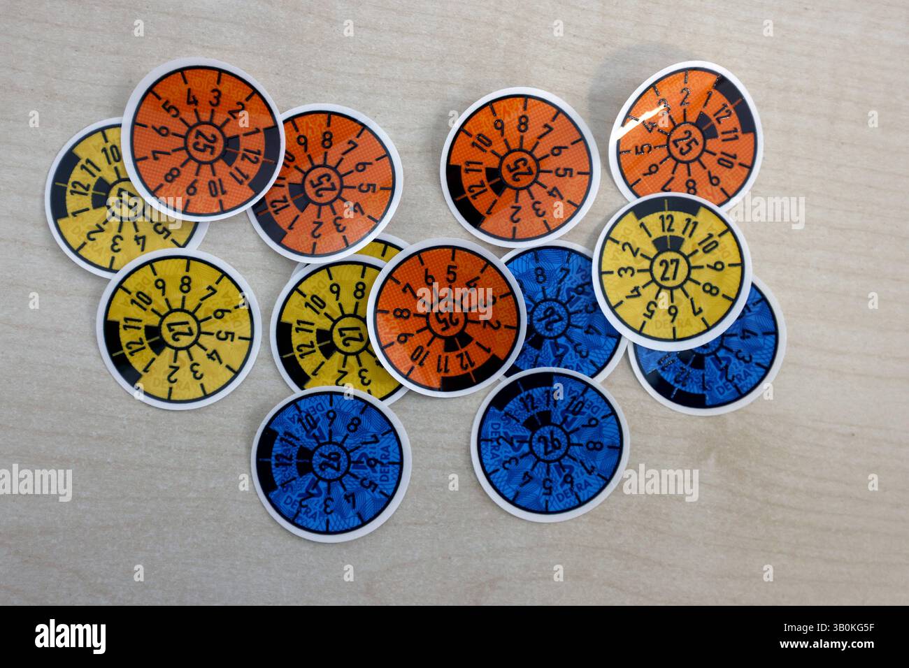 Tuev Tüv Plaketten in den Farben gelb, blau und orange liegen auf einem ...
