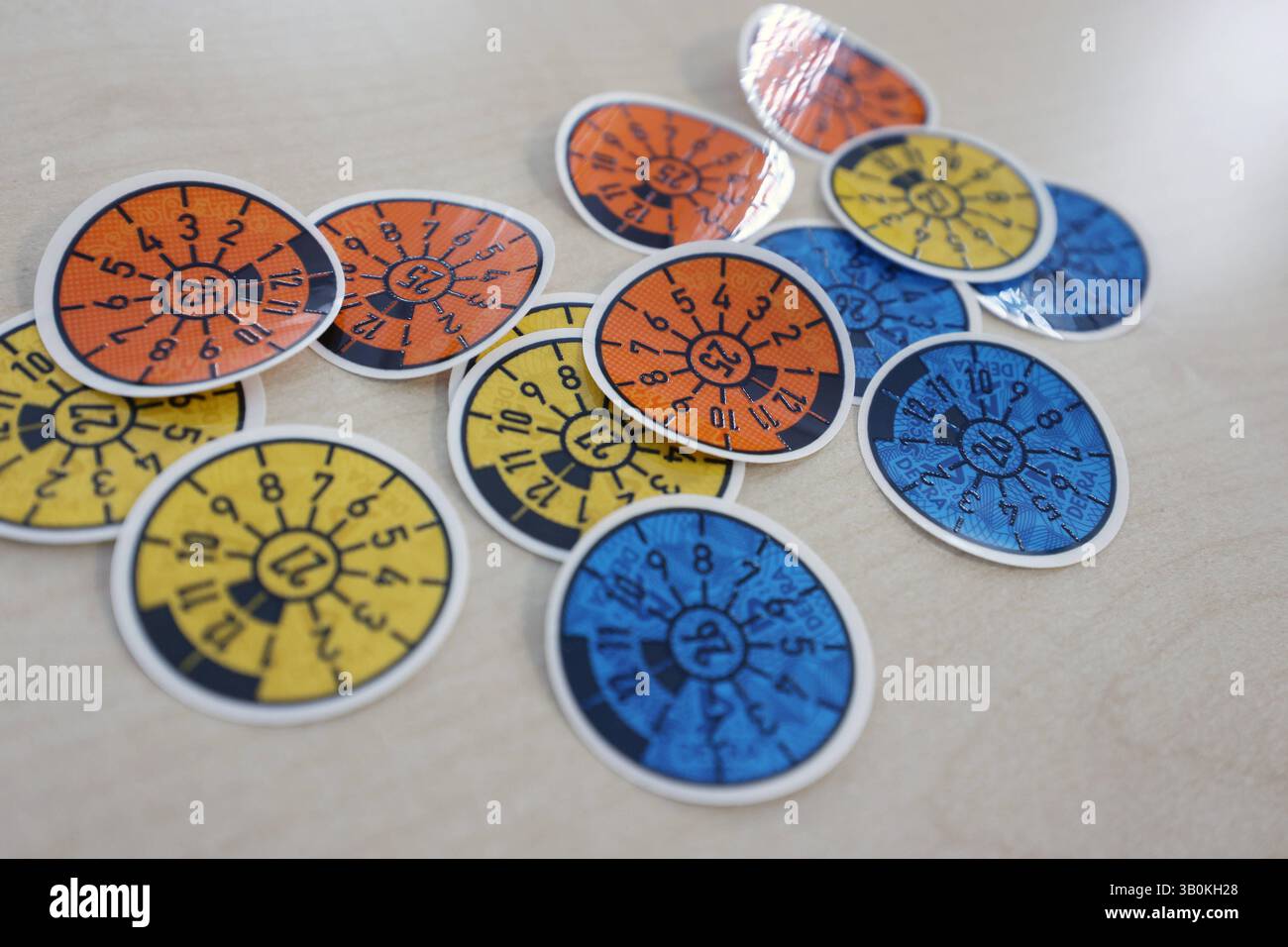 Tuev Tüv Plaketten in den Farben gelb, blau und orange liegen auf einem ...