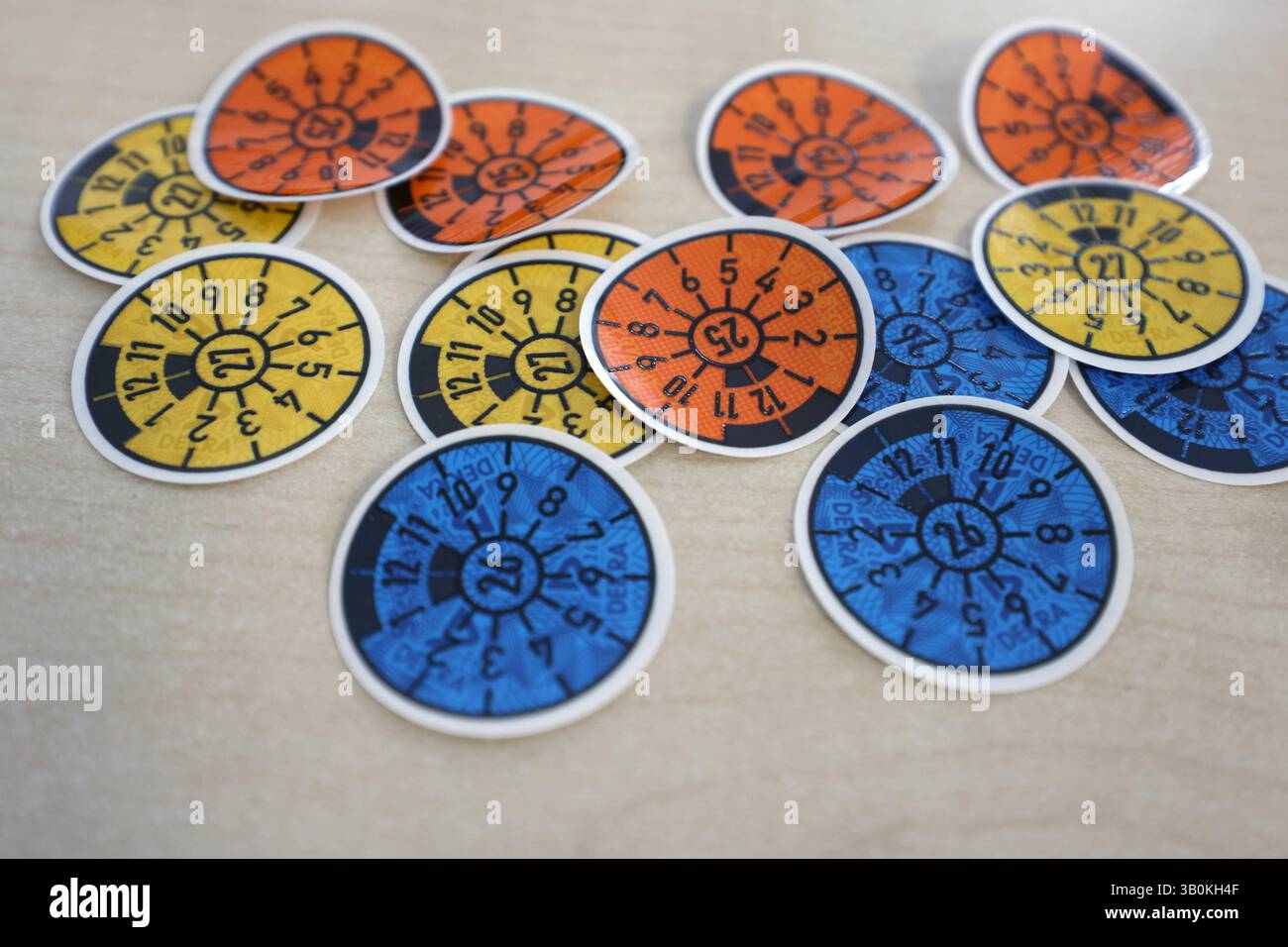 Tuev Tüv Plaketten in den Farben gelb, blau und orange liegen auf einem ...