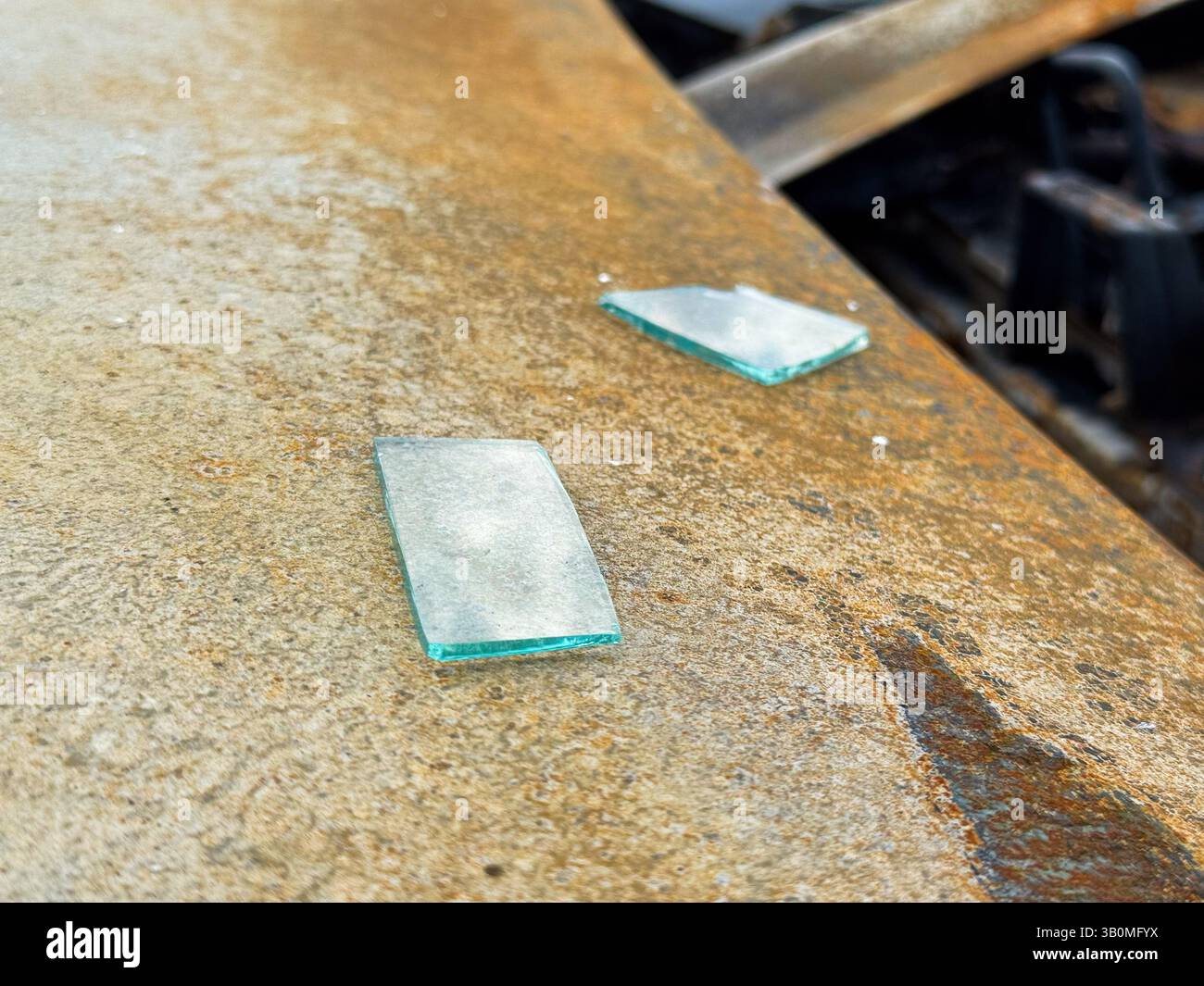 Two flat shards of broken automotive safety glass resting on the rusted ...