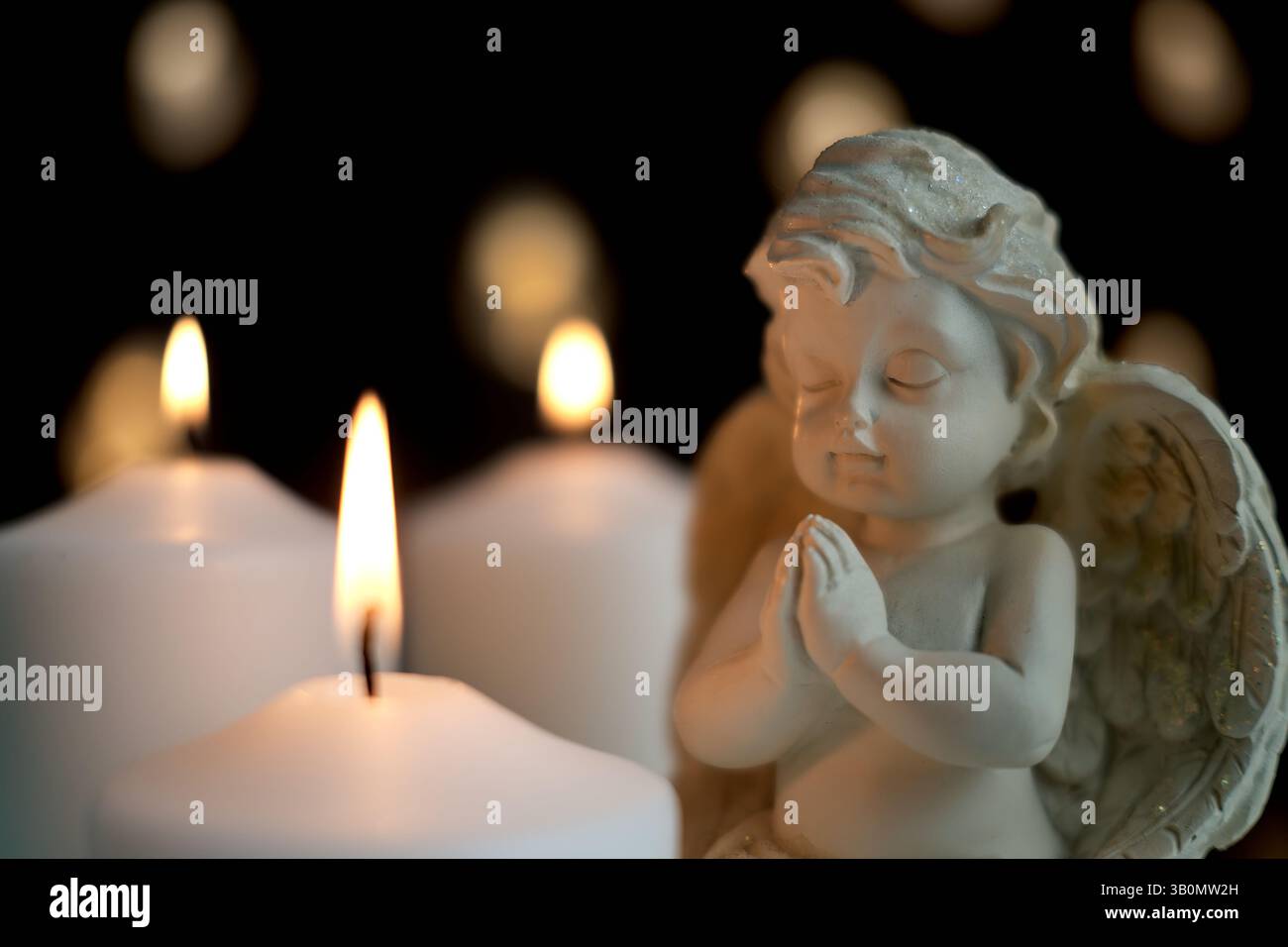Porcelain angel statue in prayer pose with folded hands, illuminated by ...