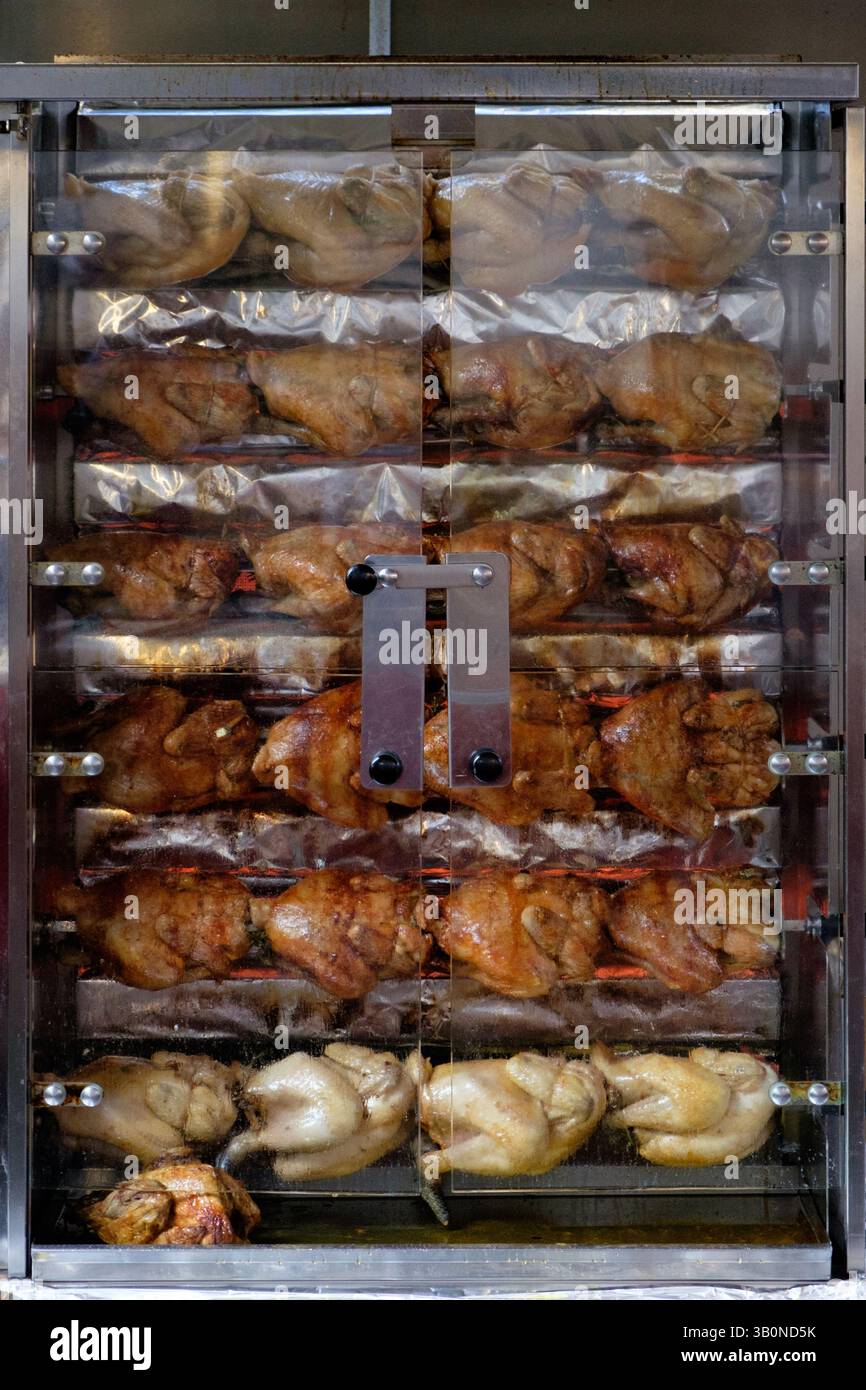 Rotisserie chicken cooks in a glass-front oven. The chickens are cooked ...