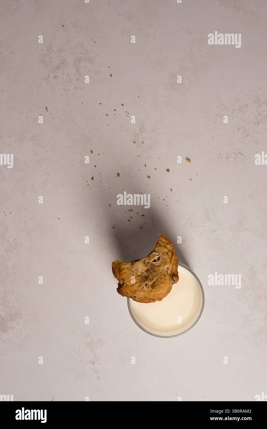 A partially eaten chocolate chip cookie resting on the rim of a glass ...