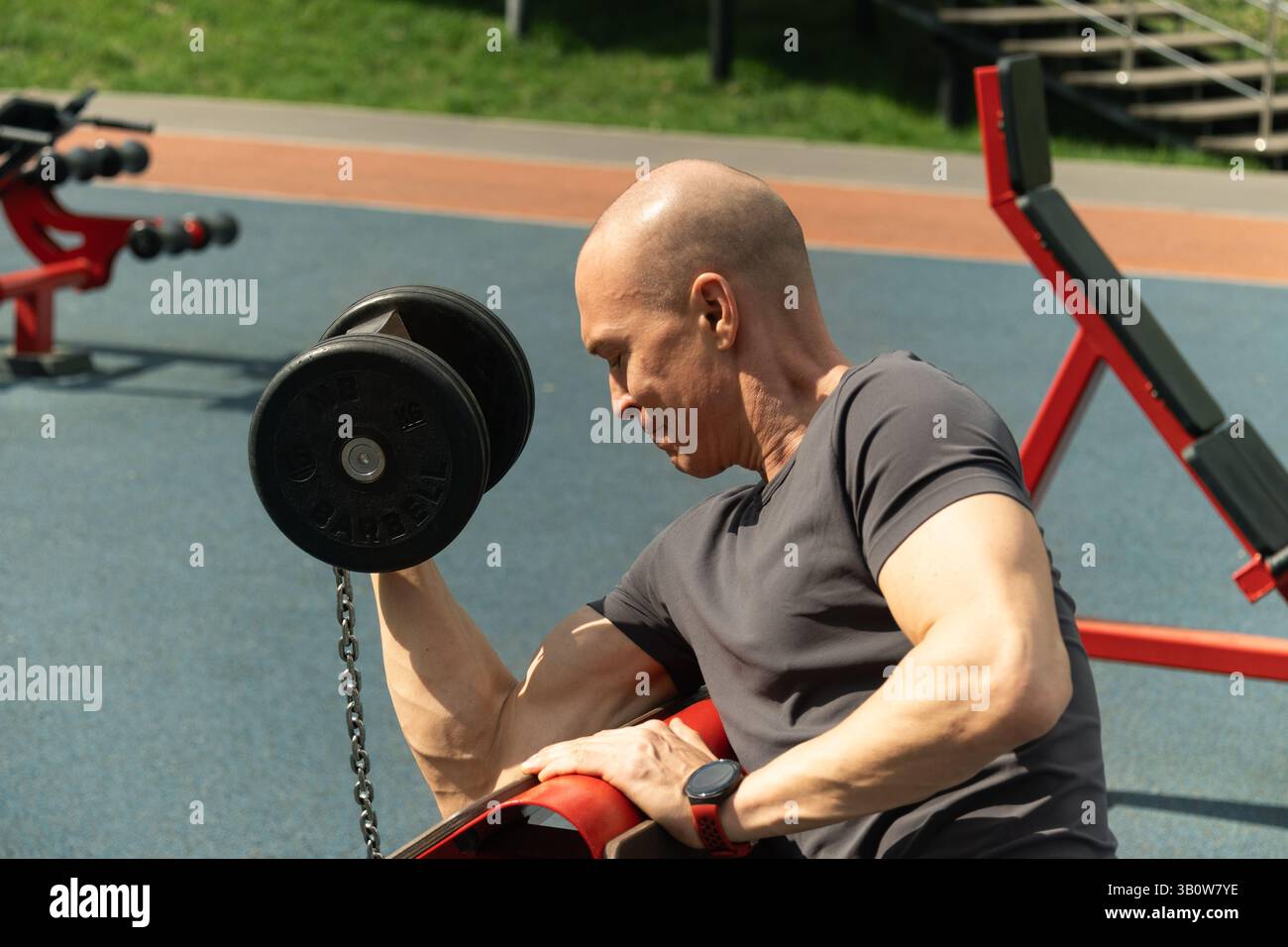 Athlete muscular man practicing with black dumbbell at outside gym ...