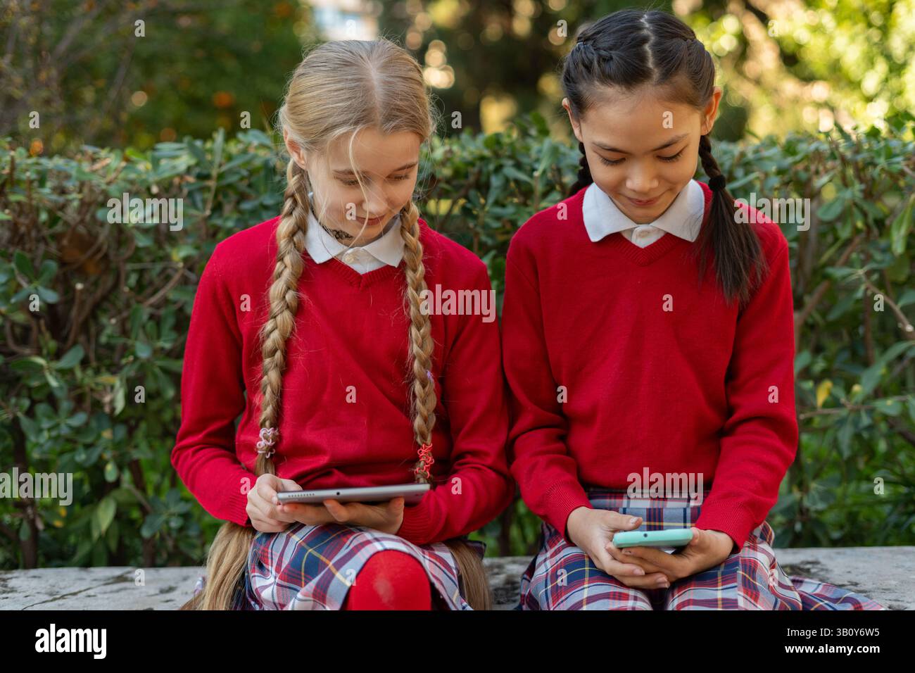 Two girls wearing school uniforms are using a tablet and a smartphone ...