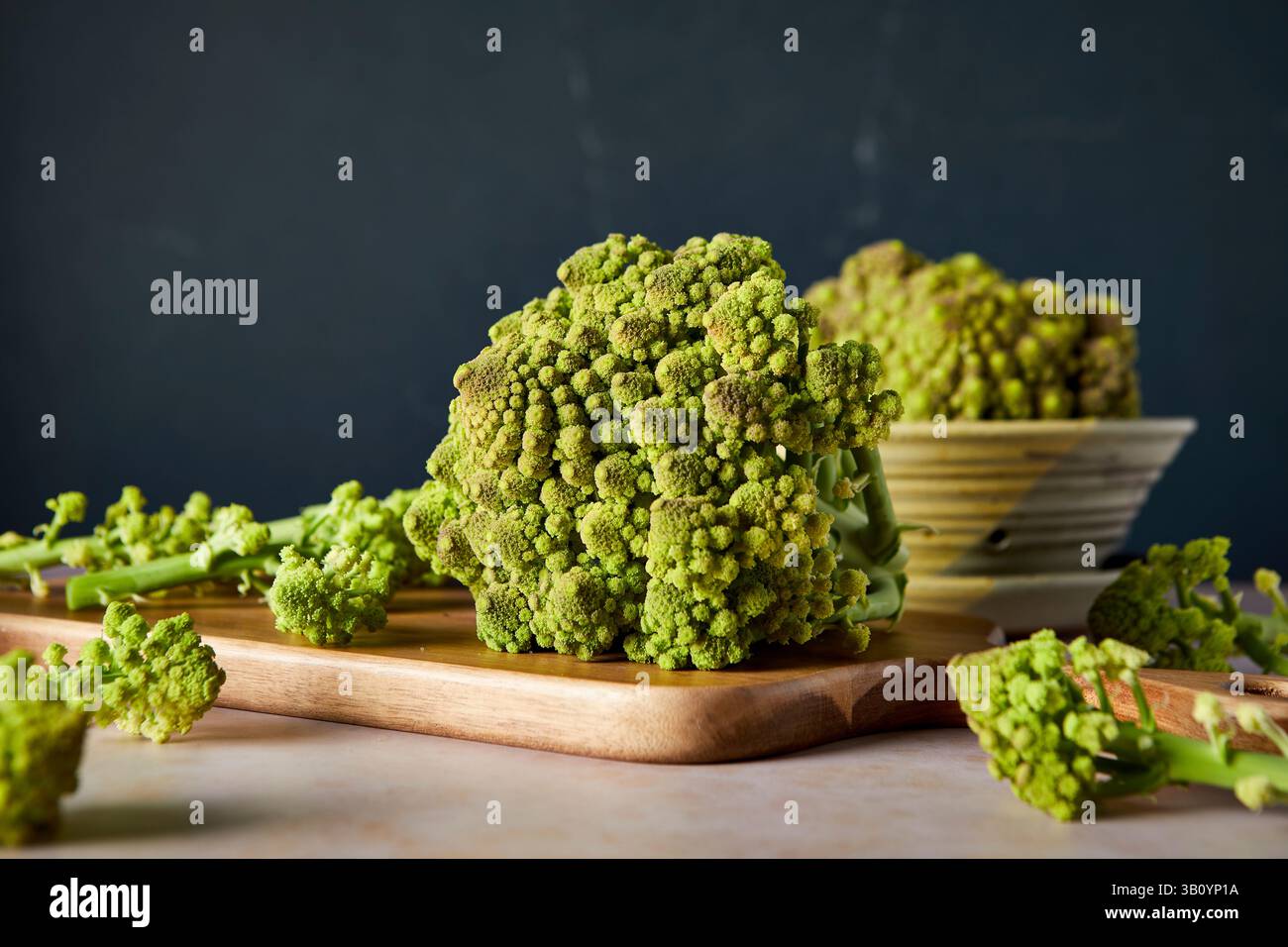 A romanesco is being cut on a wooden cutting board with another washed ...