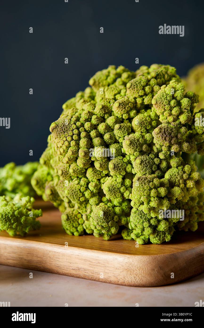 A romanesco is being cut on a wooden cutting board with another washed ...