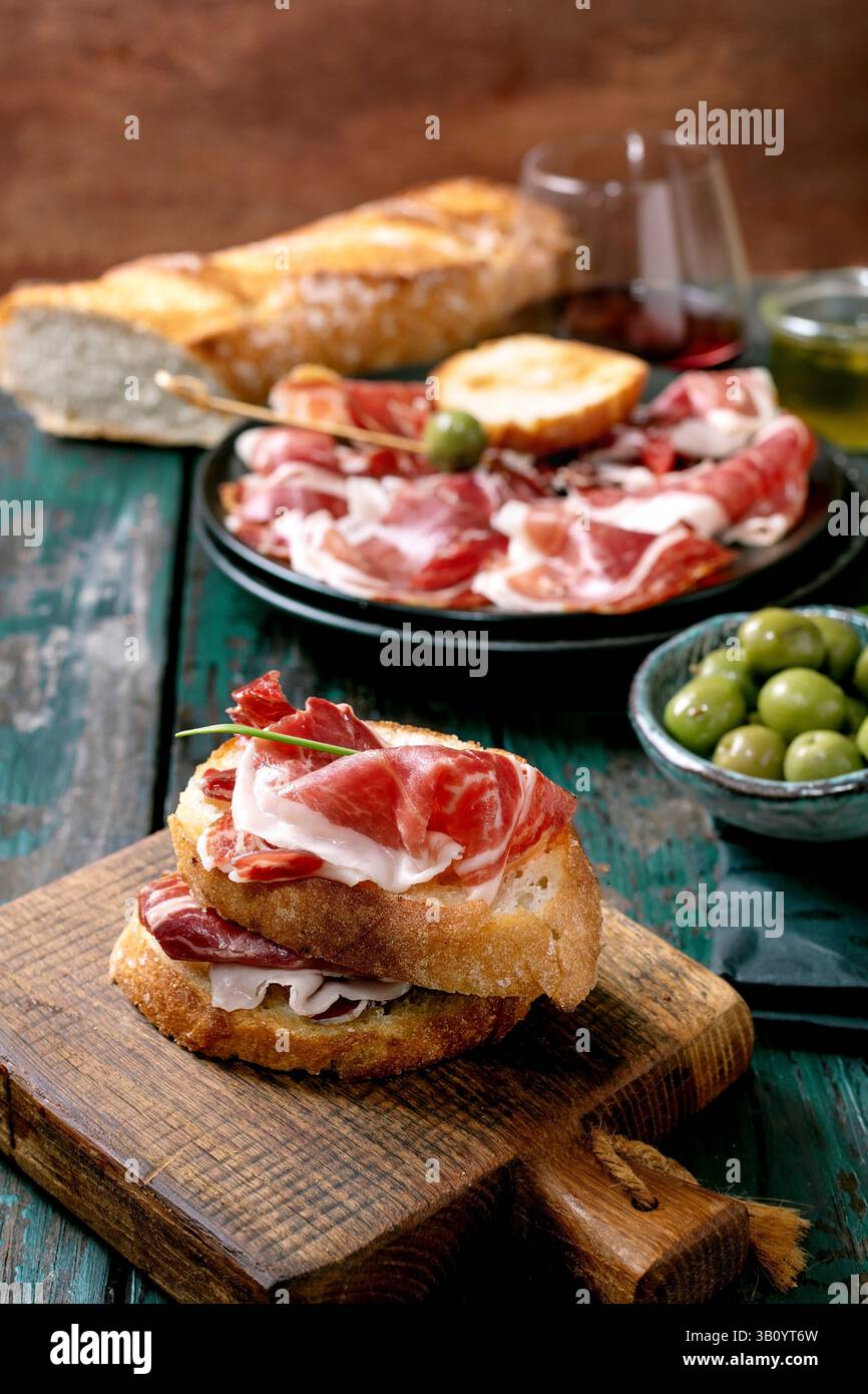 Sliced Spanish ham Jamon Iberico paleta on black plate. Bowl of green ...