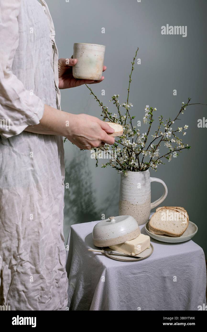 Woman white linen dress holds ceramic cup next to breakfast table with ...