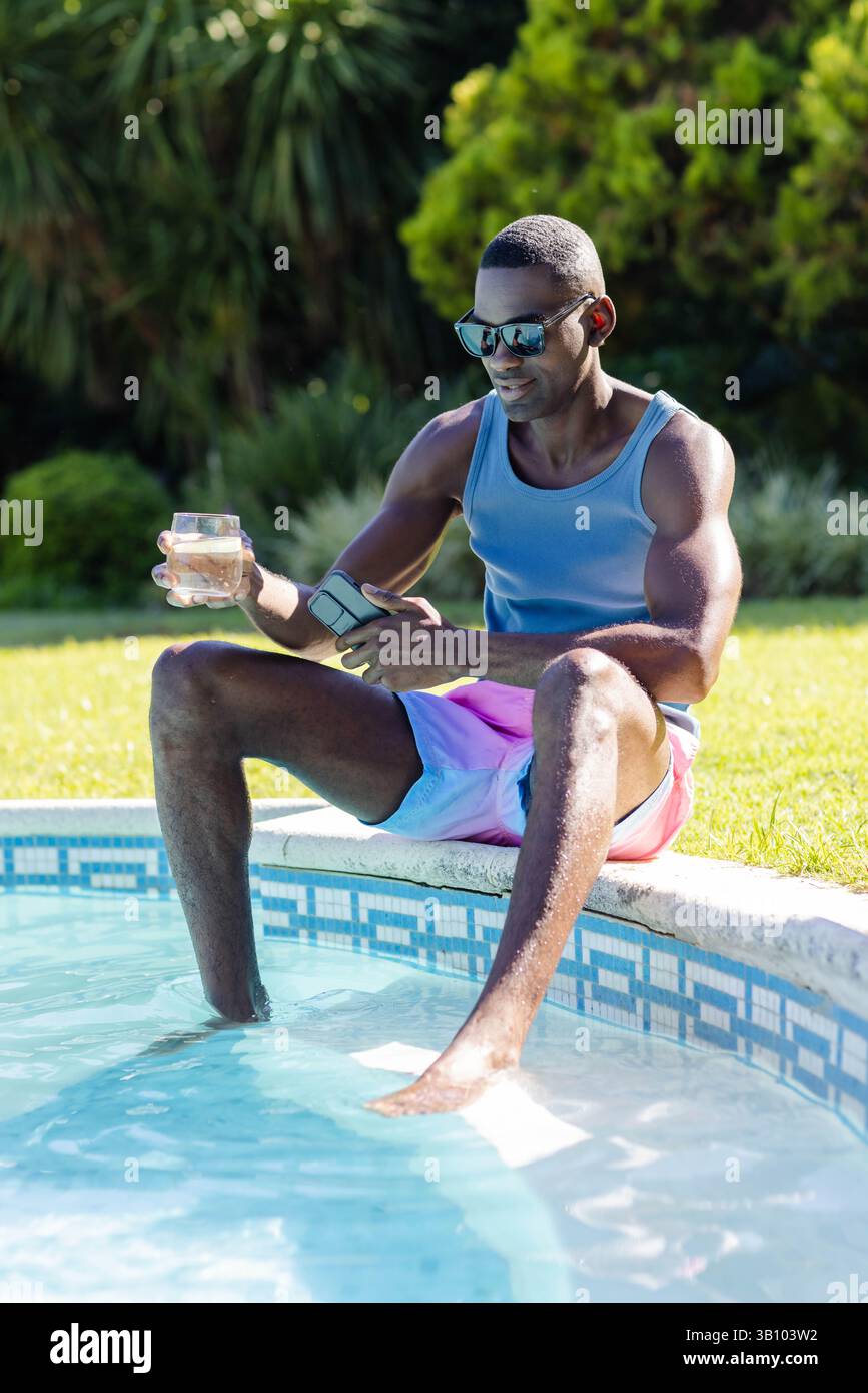 Sitting mid-adult African American man dipping legs in pool at backyard ...