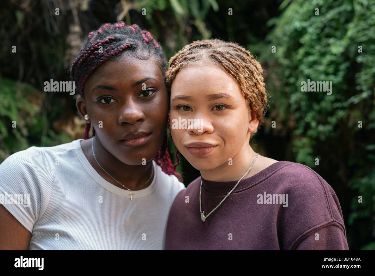 Two beautiful young women are posing together in front of a green ...