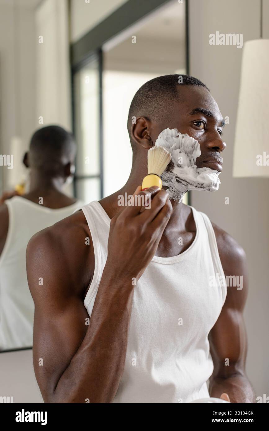Applying shaving foam African American man standing in bathroom before mirror, with shaving ...