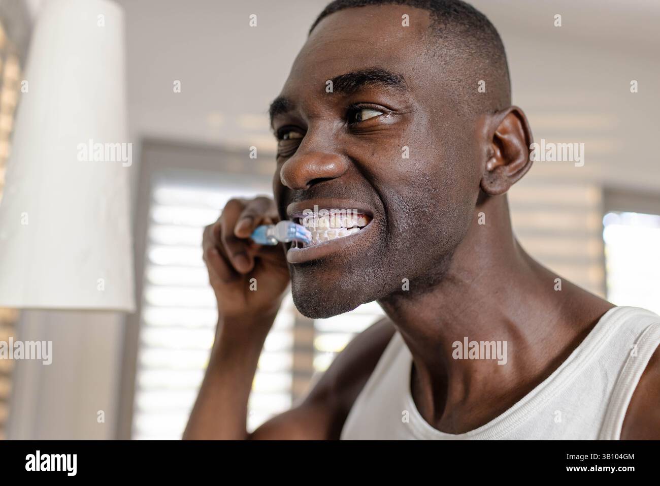 Leaning forward African American man brushing teeth at home bathroom ...