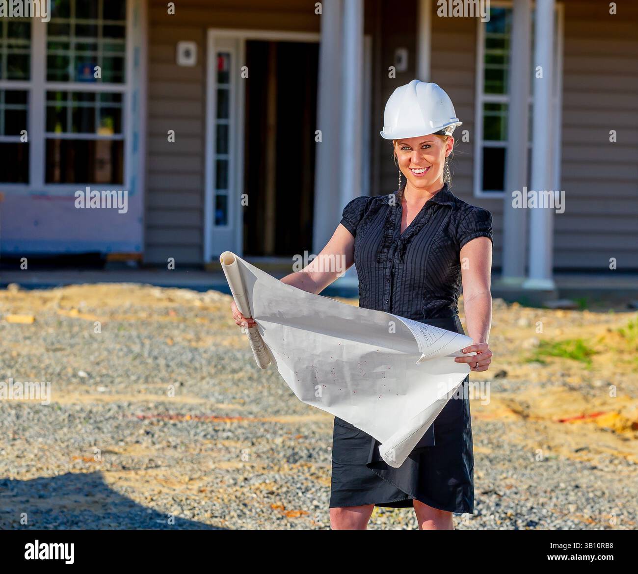 A young female construction supervisor studies house blueprints on-site ...