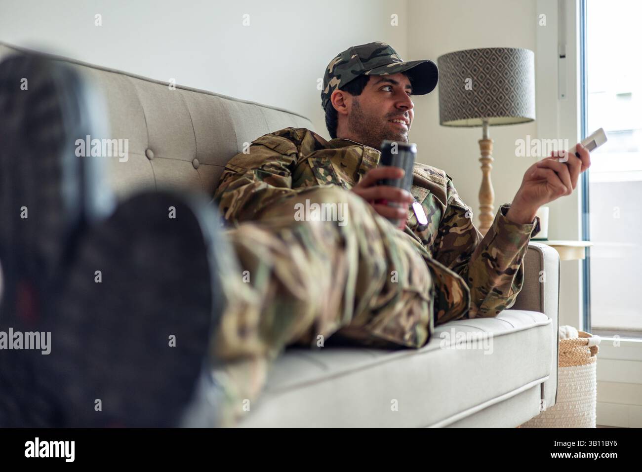 Young veteran soldier wearing camouflage uniform is lying on the sofa ...