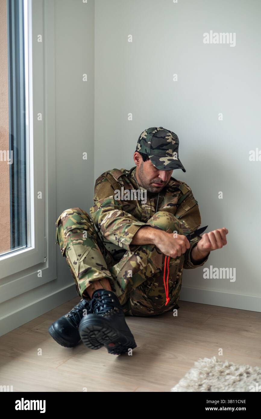 Depressed soldier in camouflage uniform sitting on floor near window ...