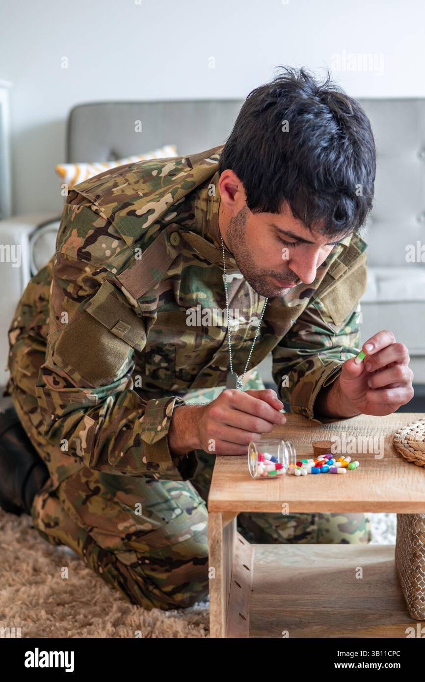 Depressed veteran soldier kneeling on the floor looking at medication ...