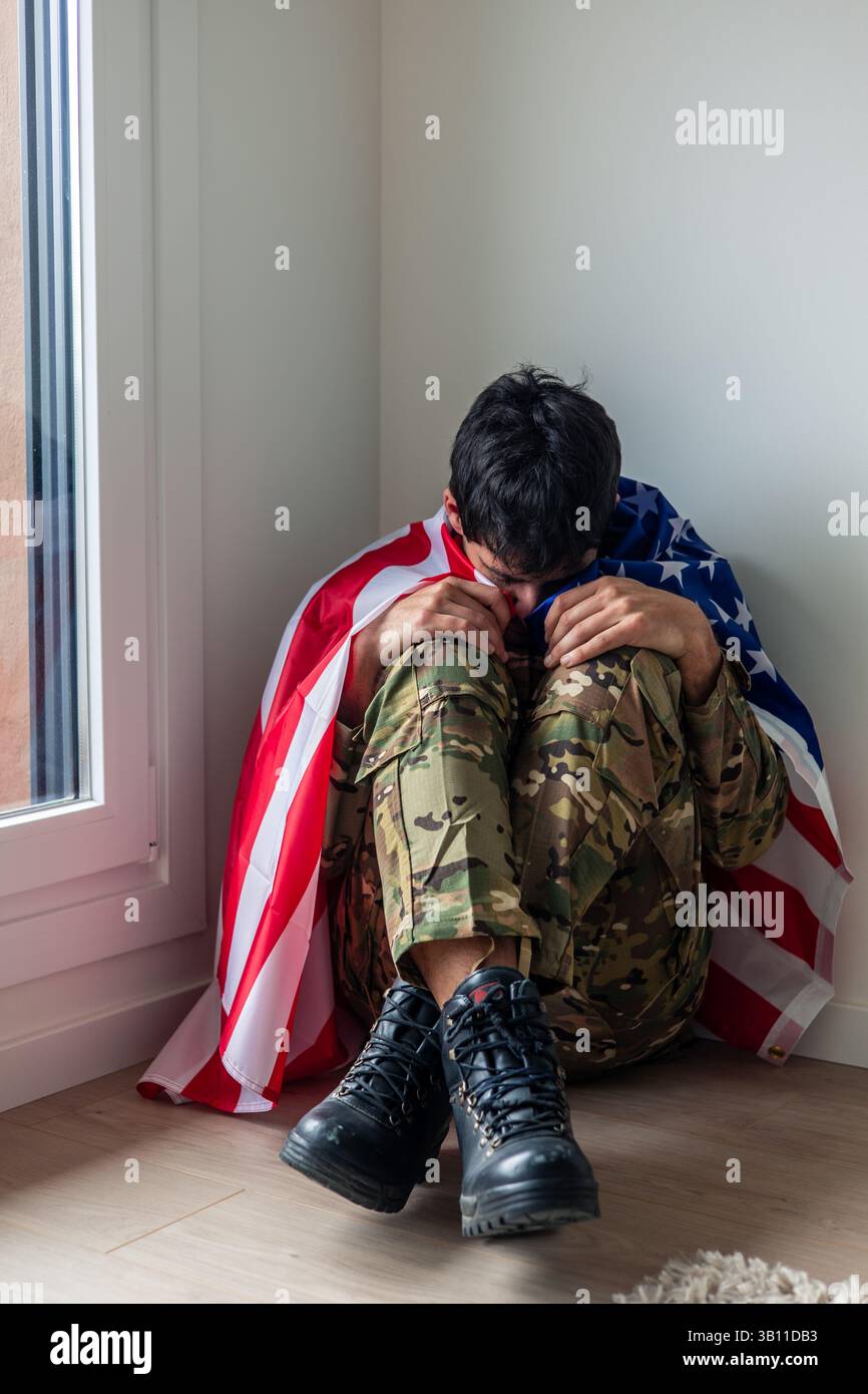 Young soldier sitting on the floor by a window, hiding his face and ...