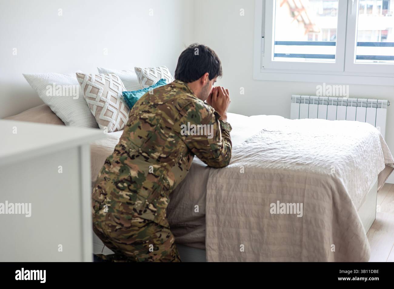 Young soldier in camouflage uniform kneeling by his bed, praying with ...