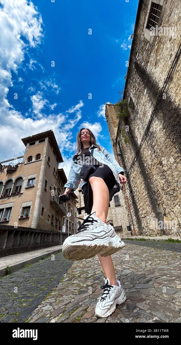 Low-angle urban portrait of a young woman in Girona, Spain, with her ...