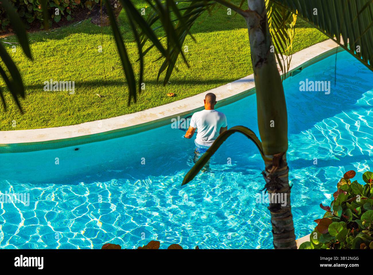 Hotel employee cleaning swimming pool in resort under bright sun ...