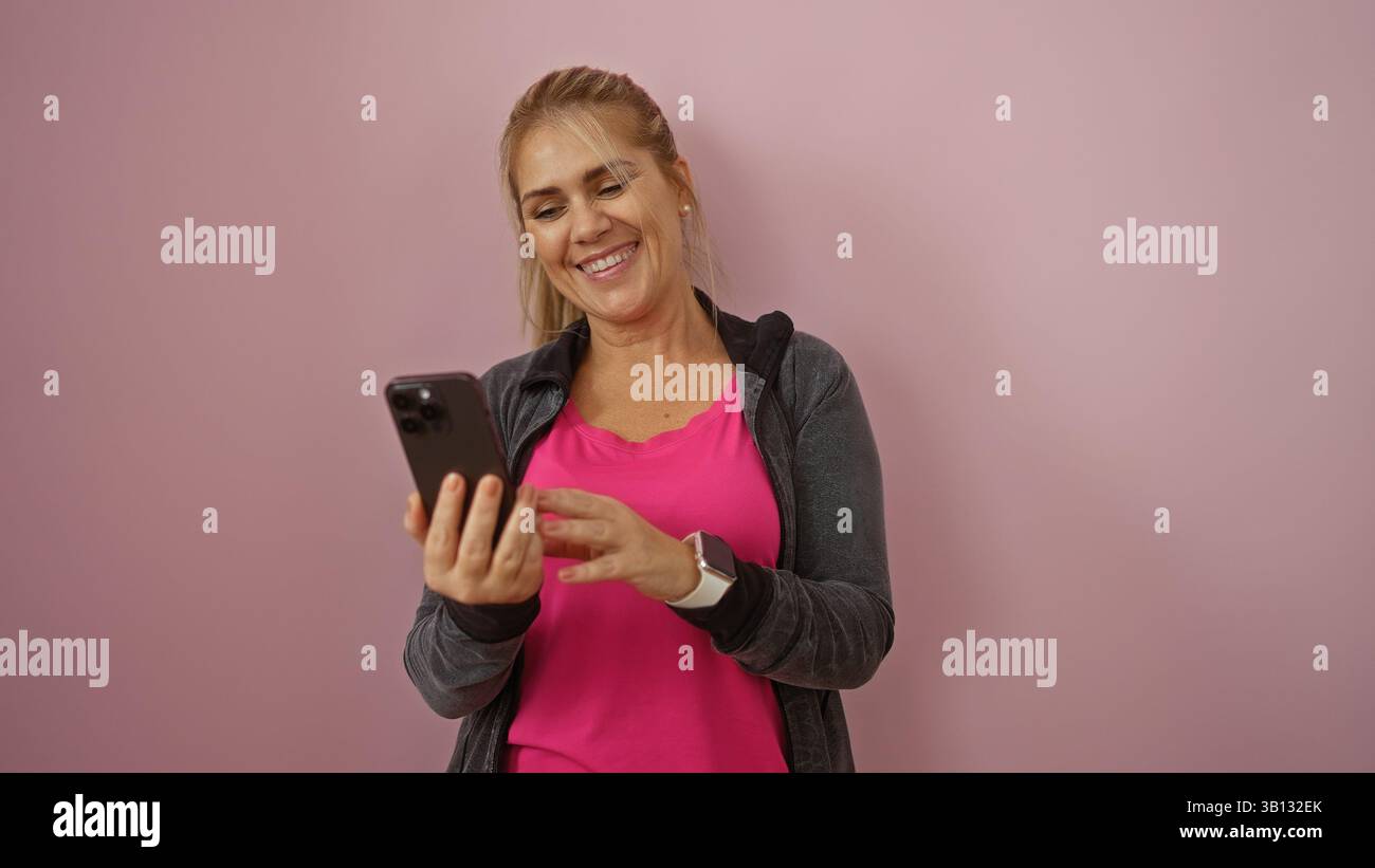 Woman smiling holding smartphone over pink background isolated while ...