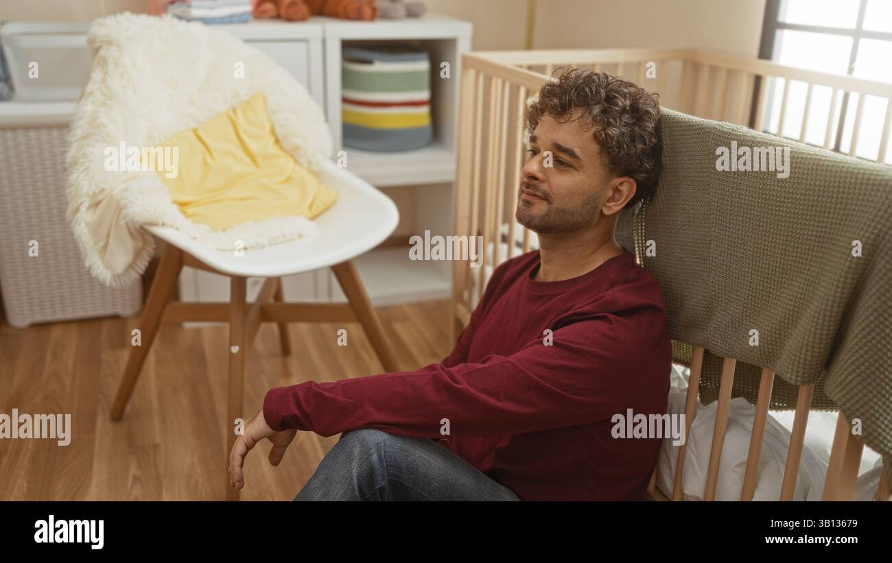 Young man indoors sitting near cradle in cozy bedroom with modern decor ...