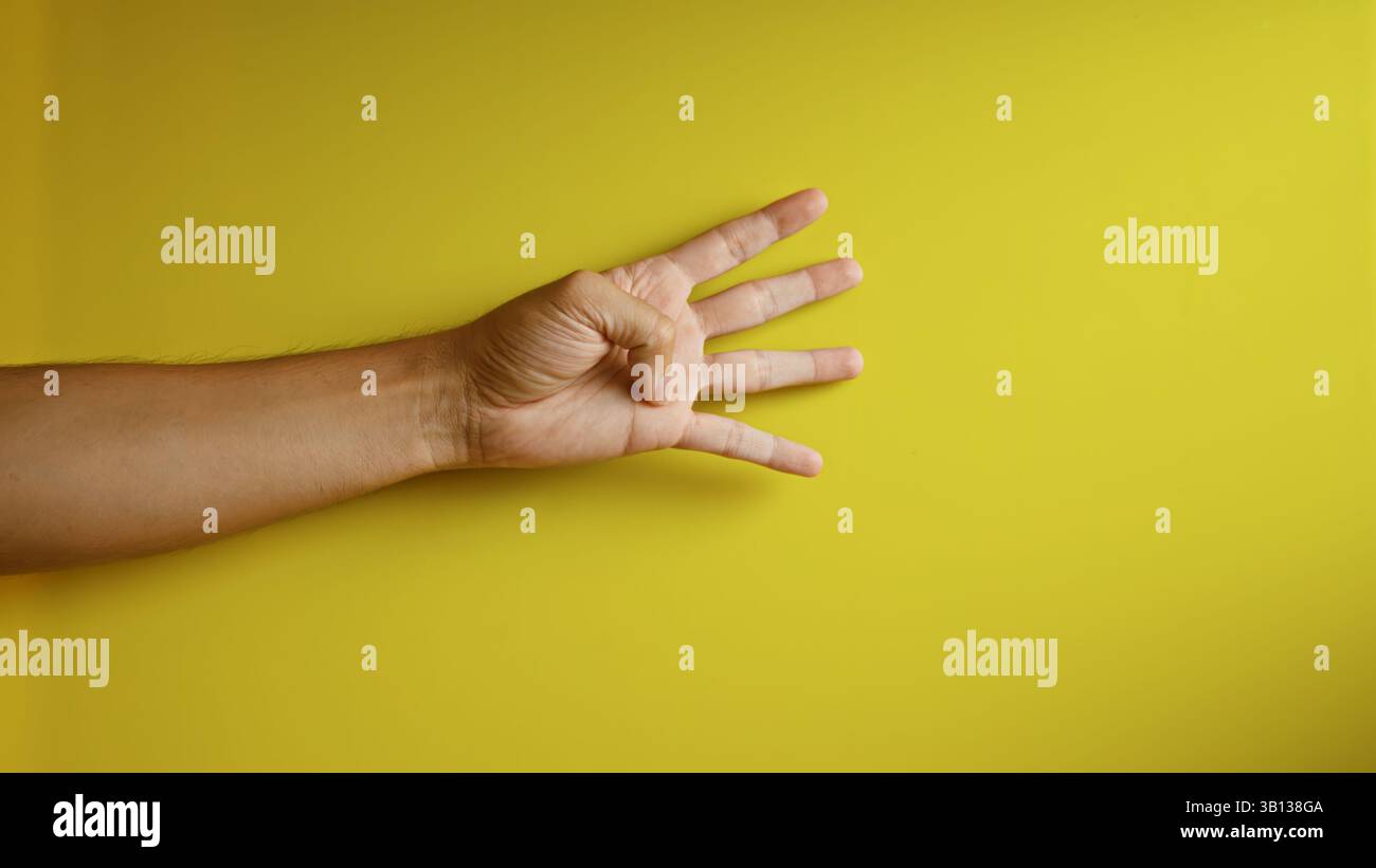 Hand showing fingers in a counting gesture against a bright yellow ...
