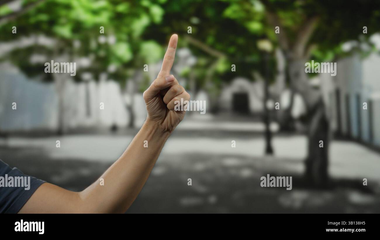 Man's hand pointing with index finger while standing on an urban street ...