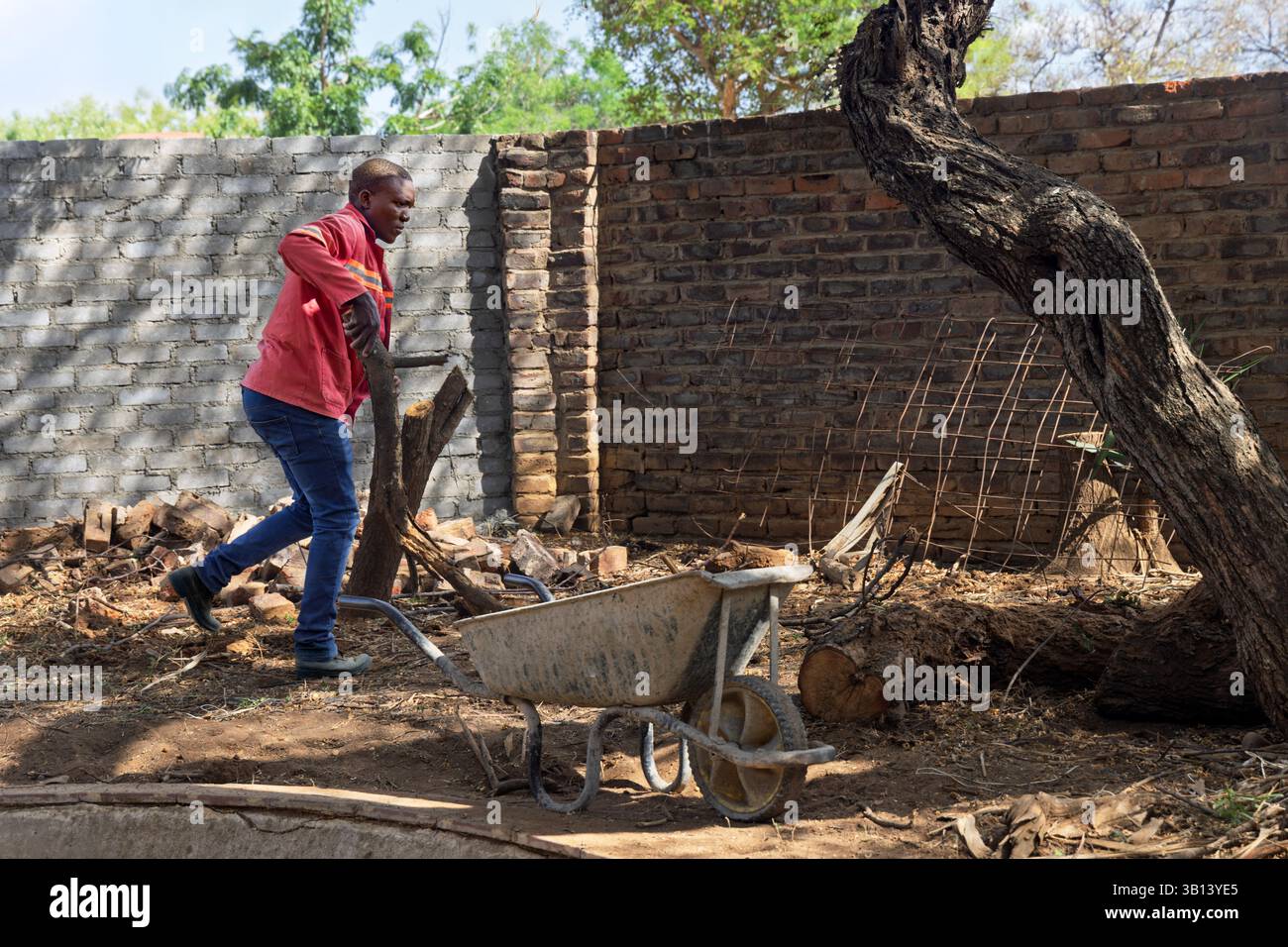 african construction worker with a wheelbarrow cleaning rubble and wood ...