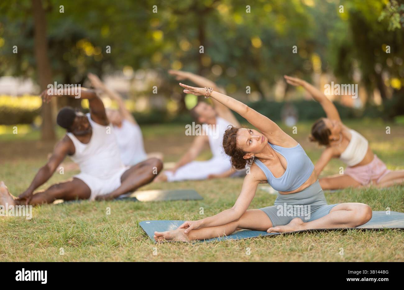 Group of people of multinational practicing hatha yoga in summer garden ...